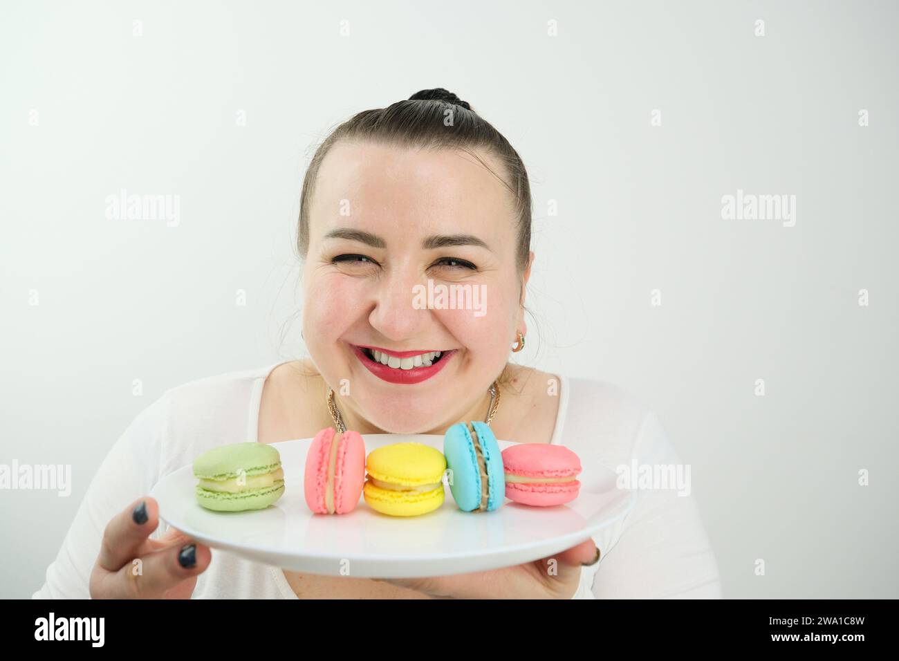 satisfied and happy woman eating macaroons on white background space ...