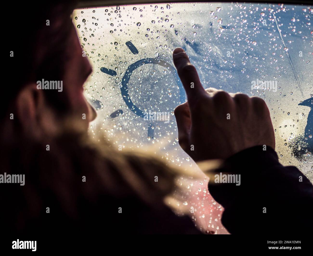A person is looking out of a car window and drawing a sun on the fogged ...