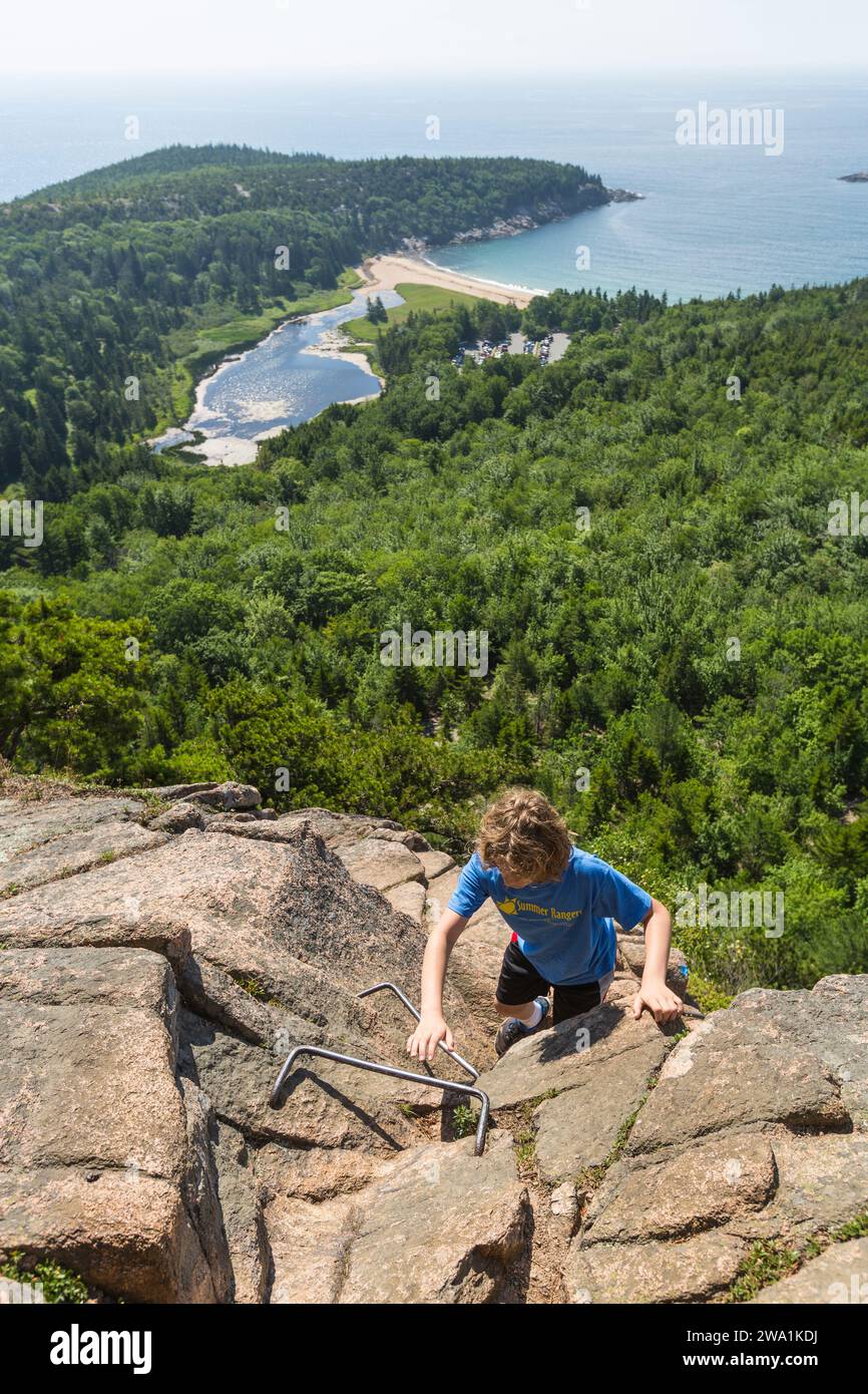 Teenage boy climbing ladder while hiking on The Beehive in Acadia ...