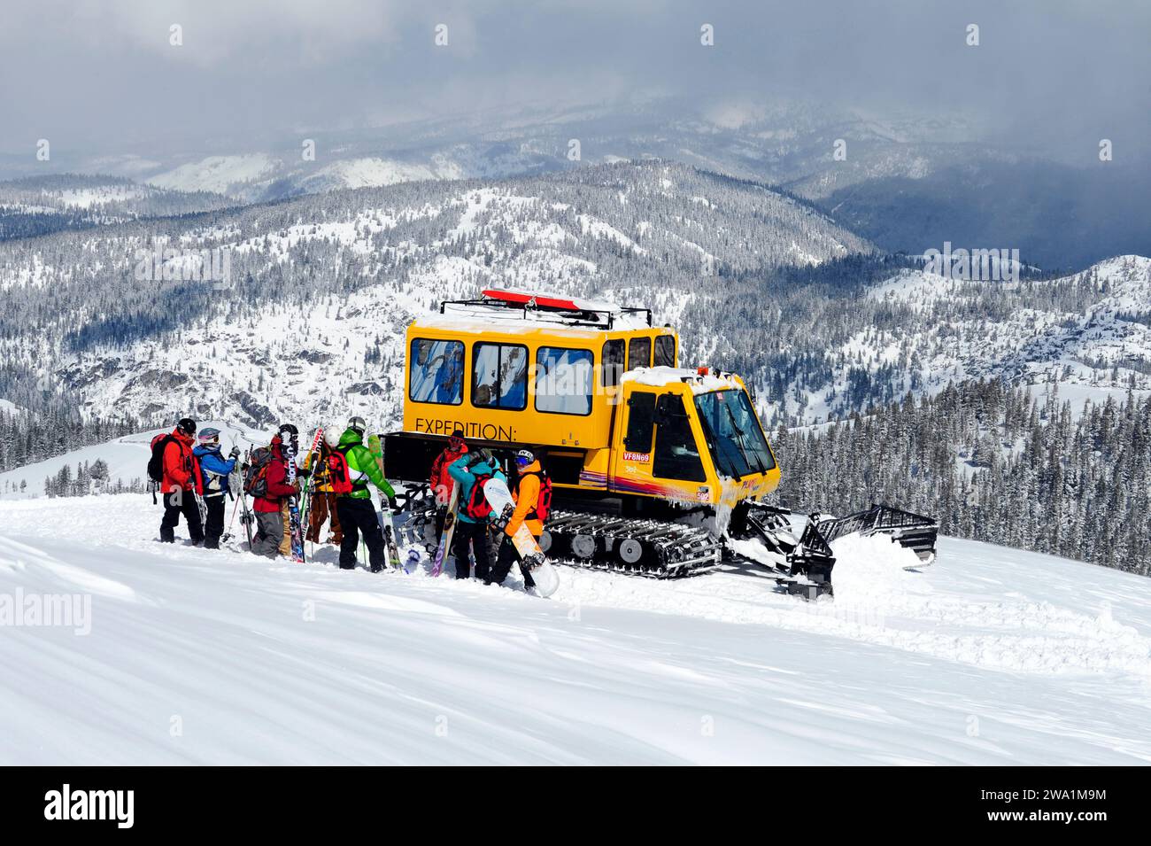 A group of skiers and snowboarders stand in front of a snow cat on a ...