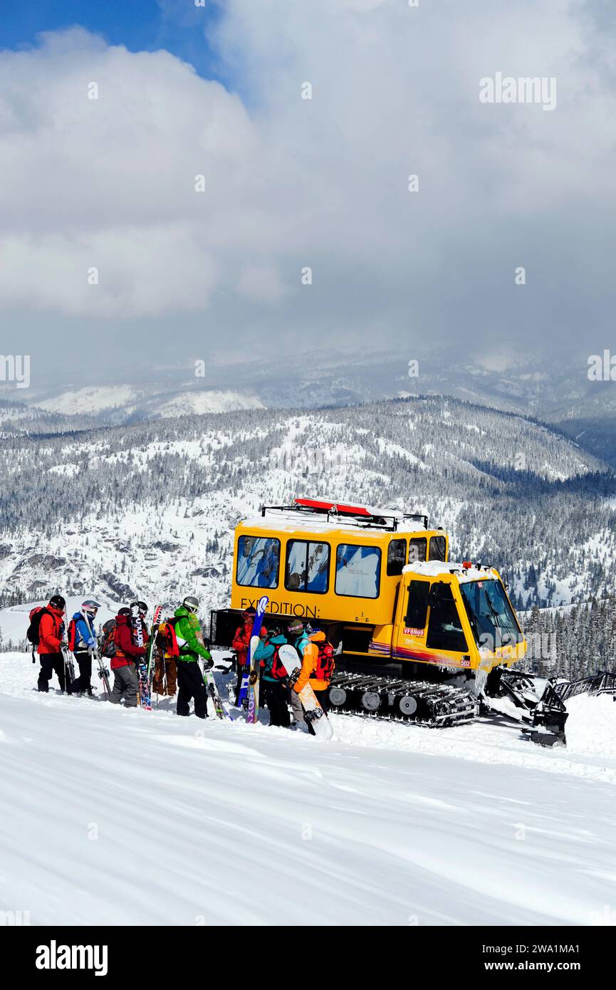 A group of skiers and snowboarders stand in front of a snow cat on a ...