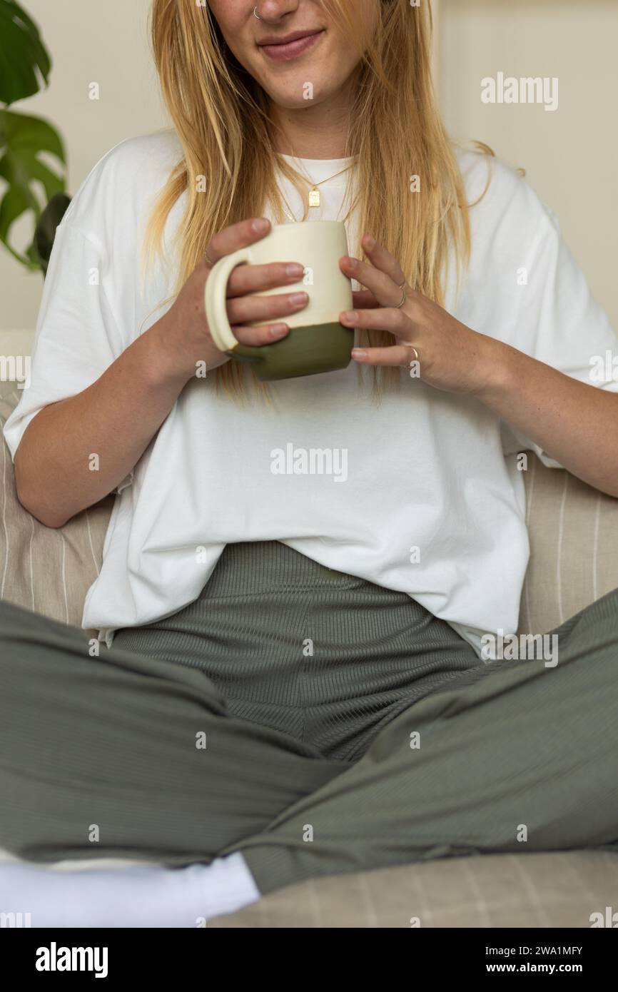 Girl enjoys morning coffee, lounging on her bed in comfortable clothes ...