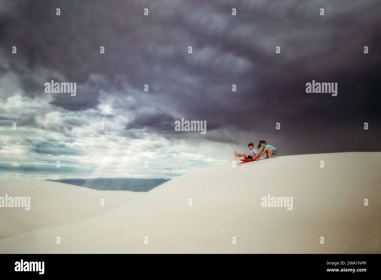 Two children sledding on white sand with storm clouds above Stock Photo ...