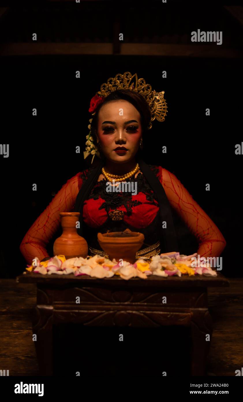 An Asian woman in a red dancer's dress is sitting at a ritual offering ...