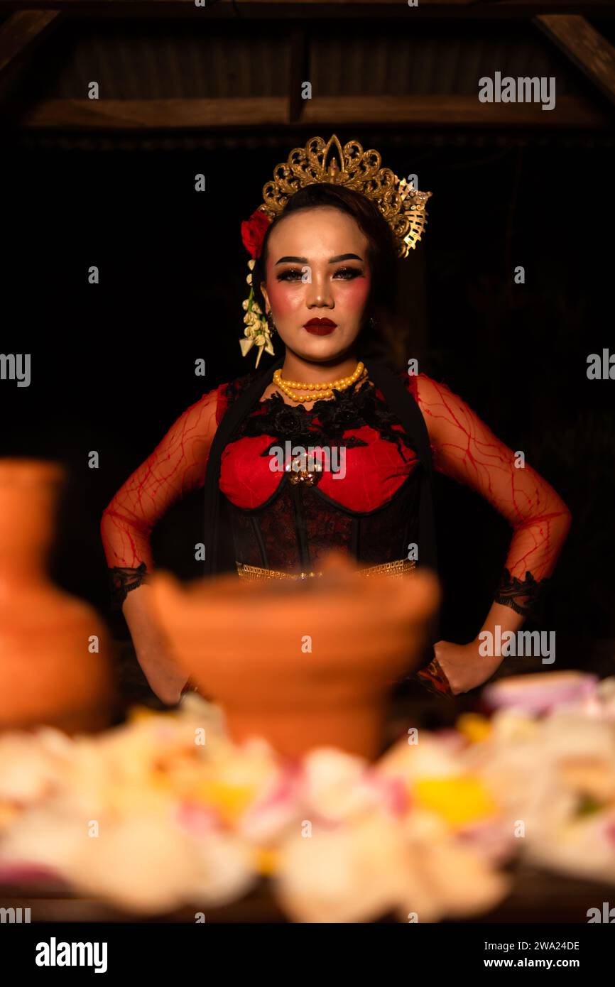 An Asian woman in a red dancer's dress is sitting at a ritual offering ...