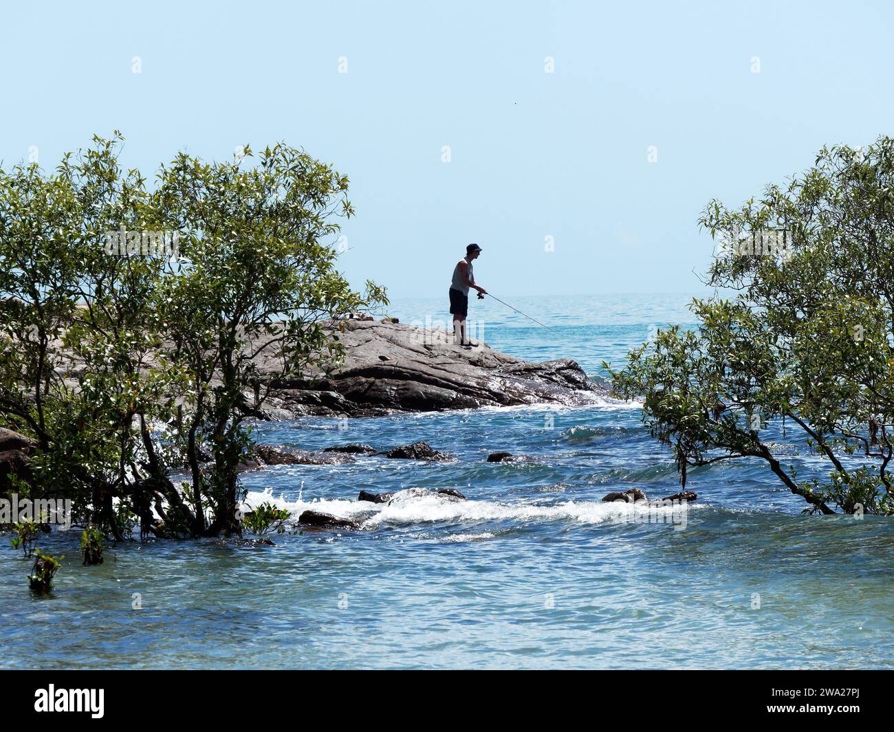 View of a man fishing from the rocks at the end of the Four Mile Beach ...