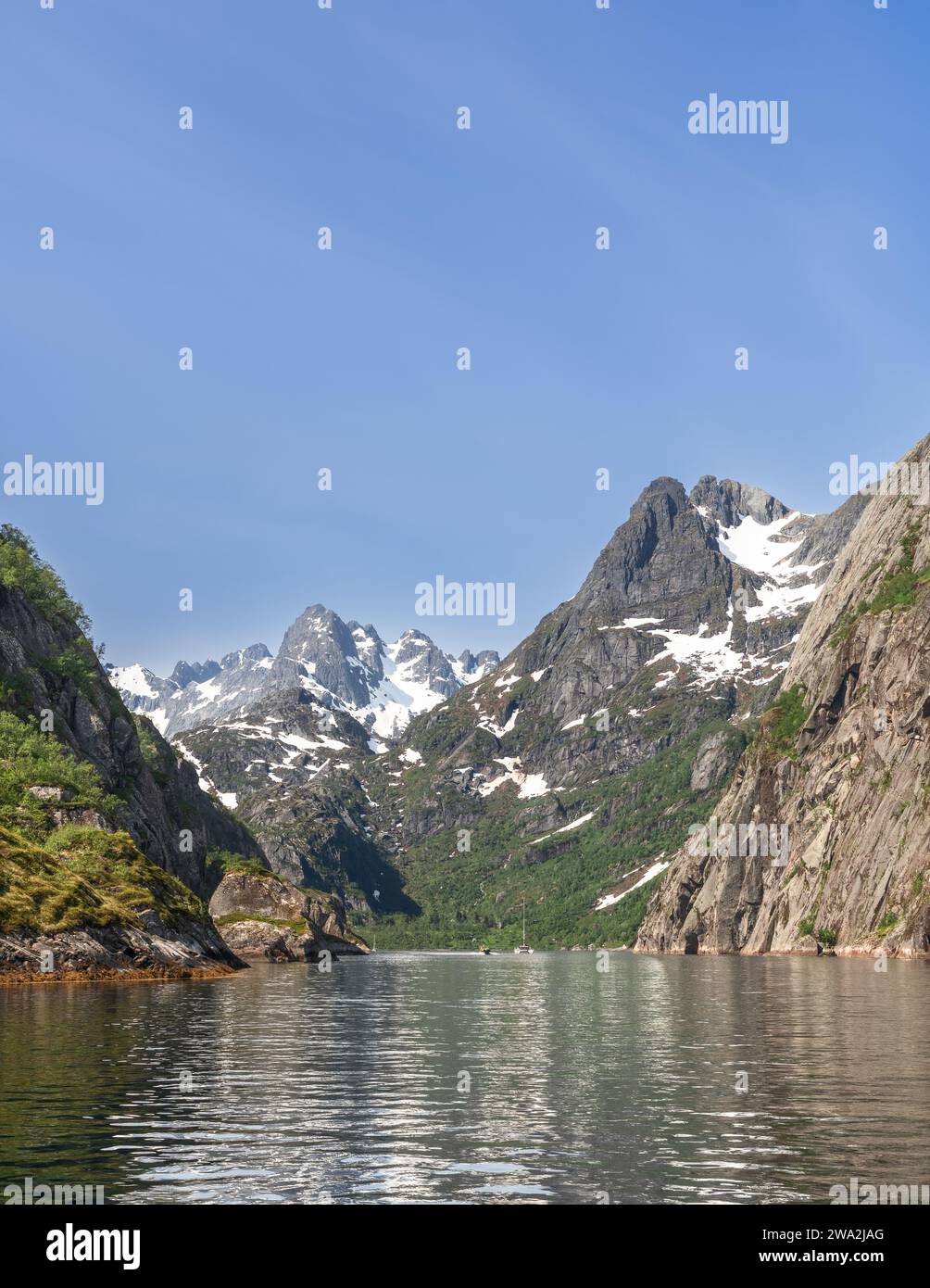 The tranquil waters of Trollfjorden reflect the rugged cliffs and snow ...