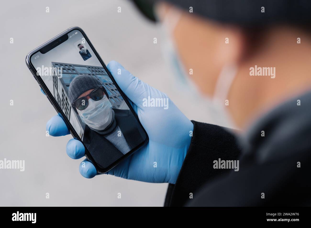 Person in gloves and mask holding a phone during a video call ...