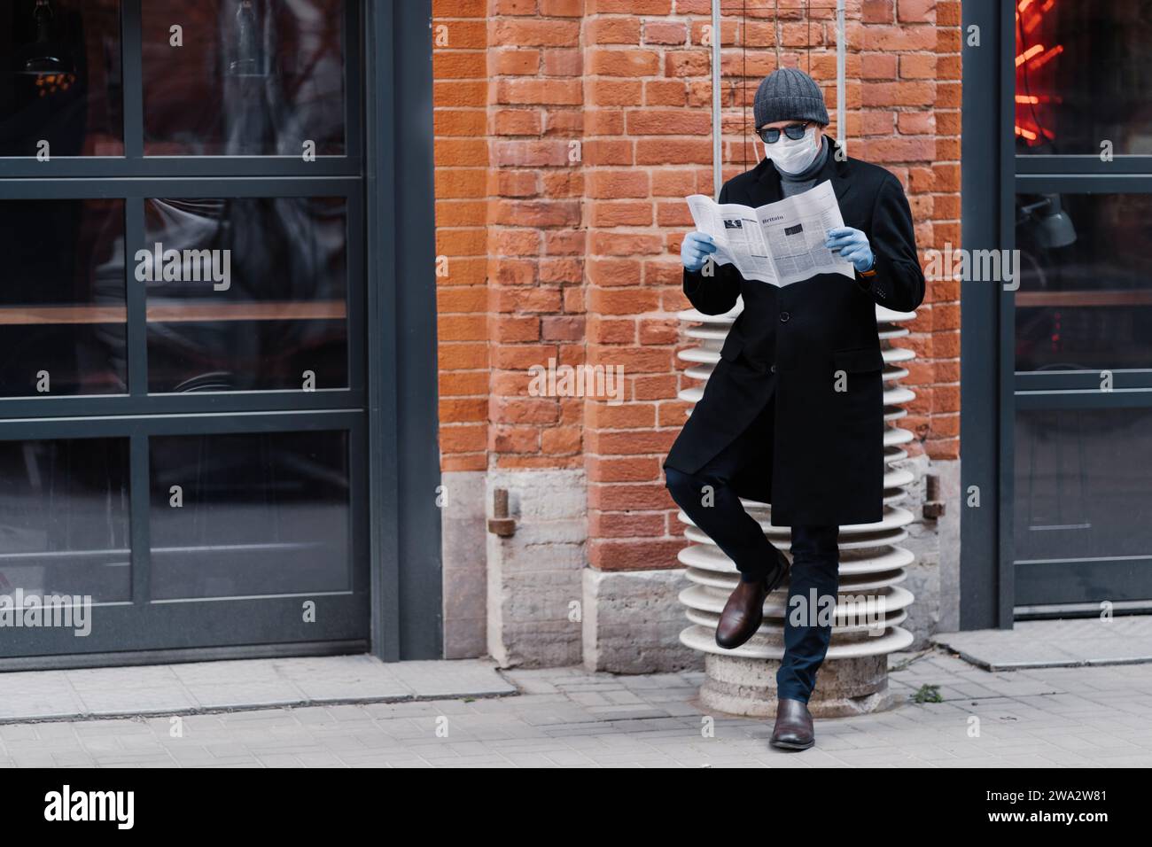 Man in a stylish winter outfit leaning against a column reading a ...