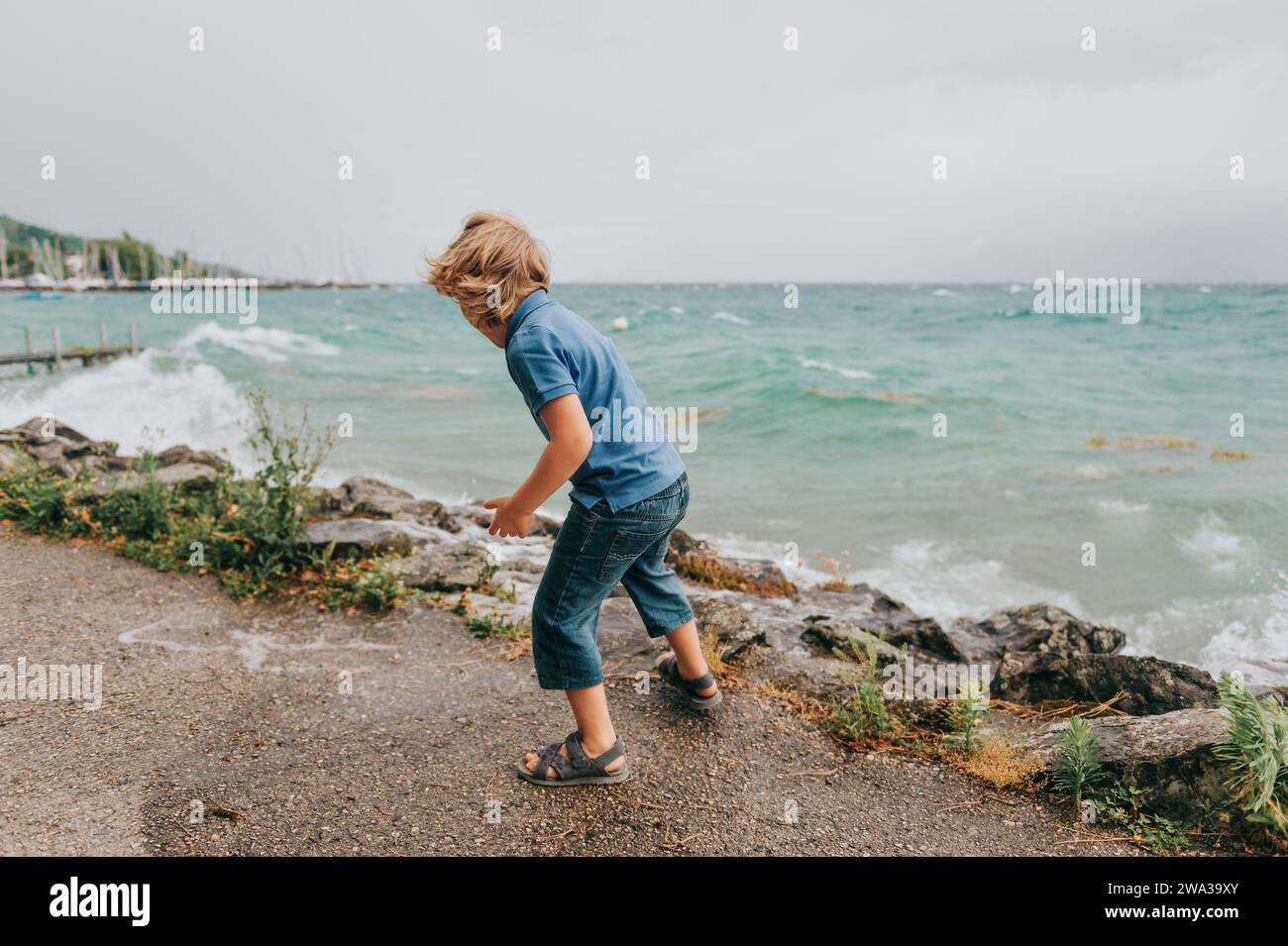 Sweet little boy playing by the lake on a very windy day wearing blue ...