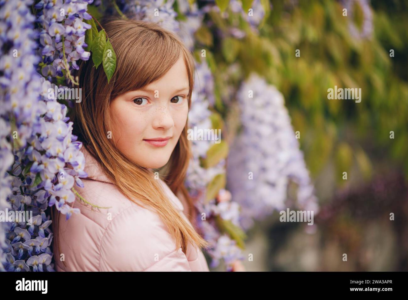 Spring portrait of adorable 9-10 year old kid girl posing in wisteria ...