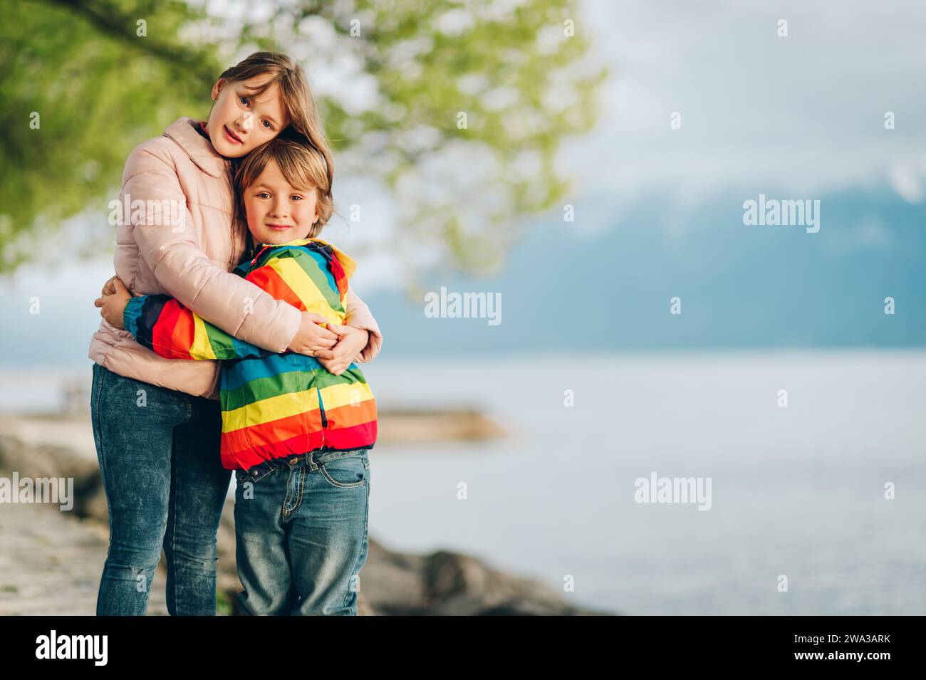 Two little kids playing together by lake Geneva on a cold day, hugging ...