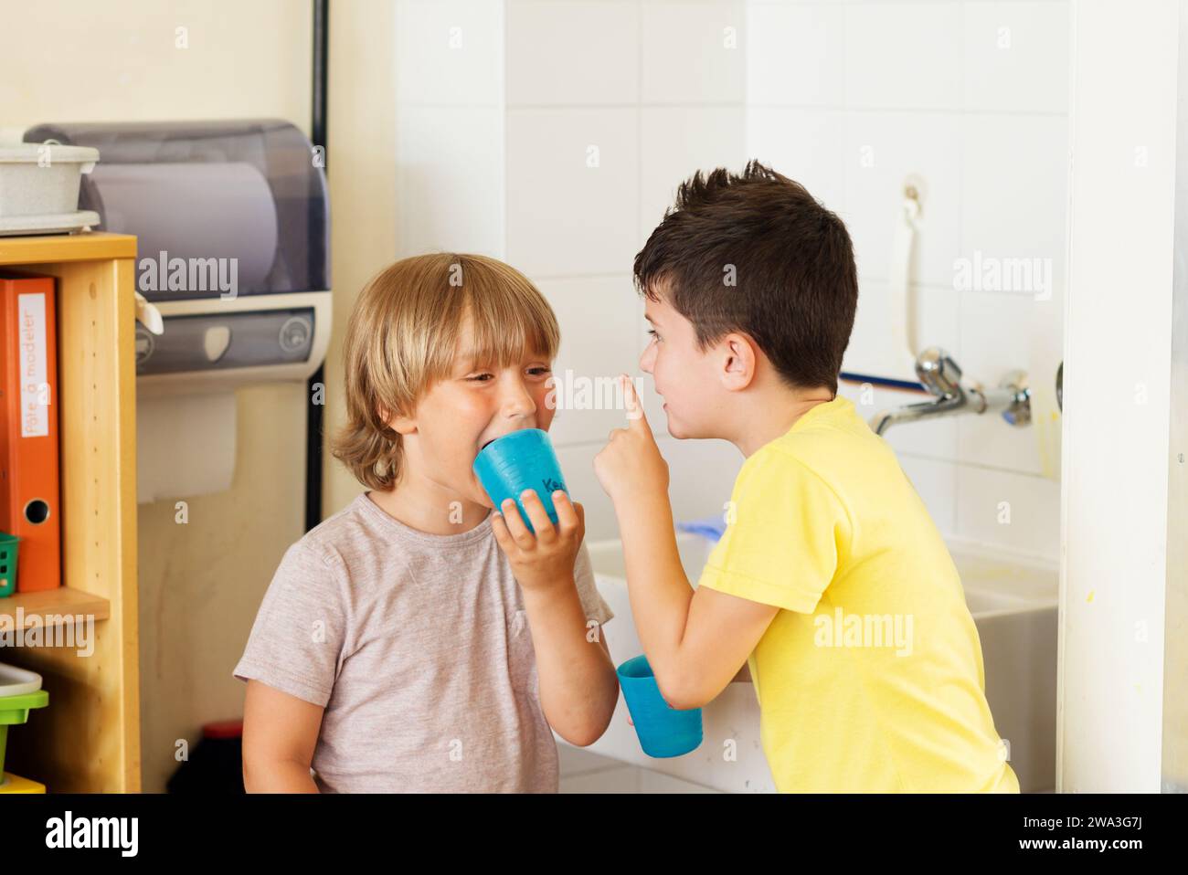 Two kids in classroom, boys drinking water in school, holding plastic ...