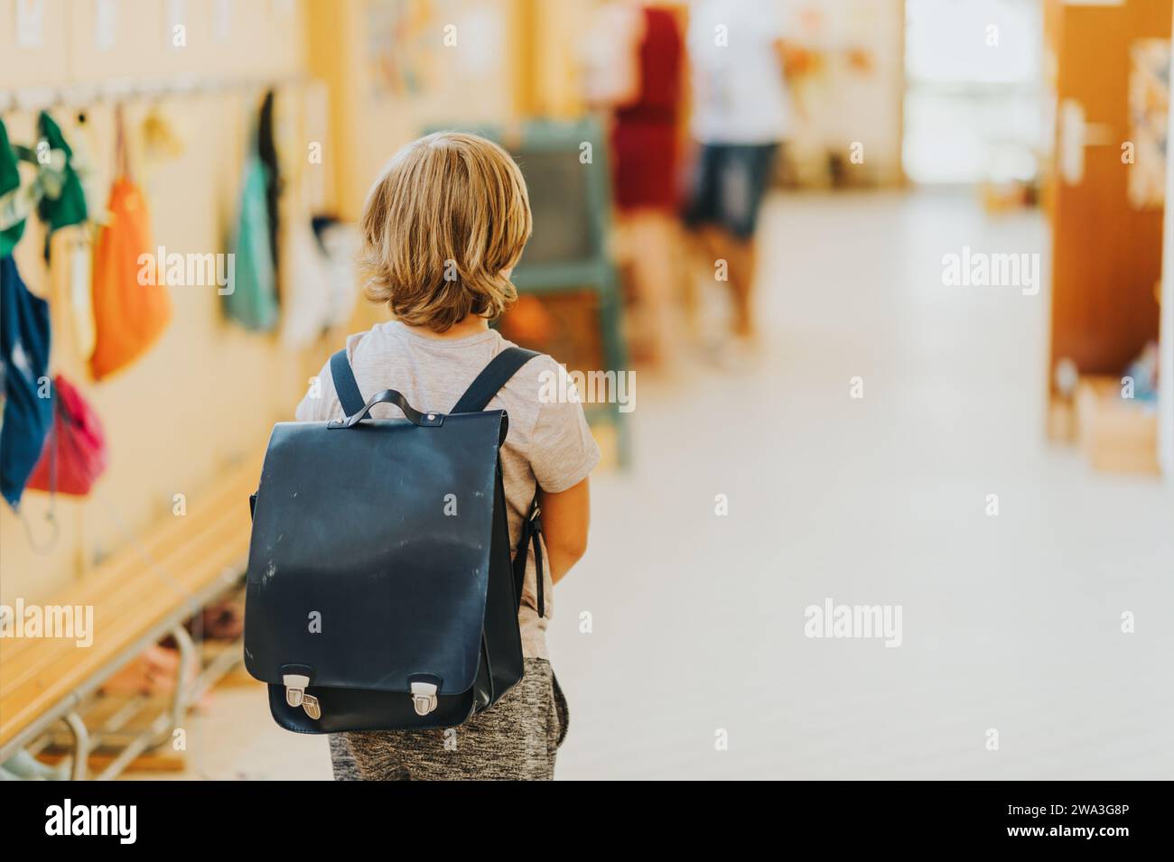 Child standing in school hallway, wearing old vintage back pack, back ...