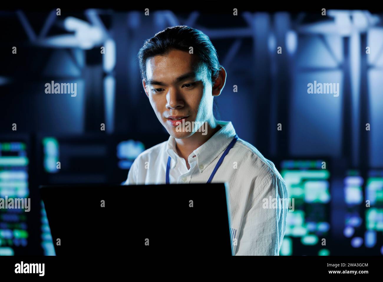 Asian man between server hub rows providing processing resources for businesses worldwide ...