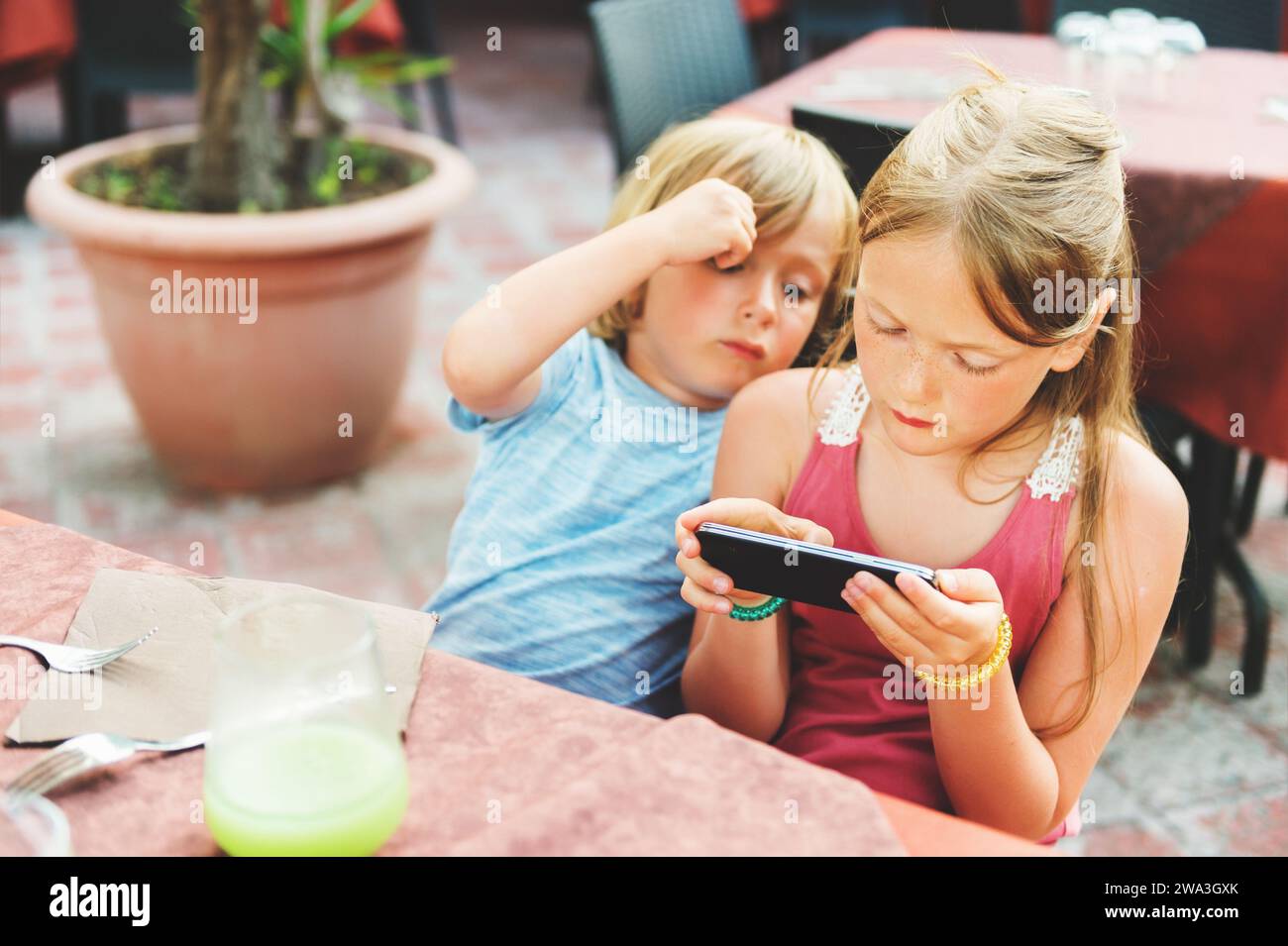 Two kids playing electronic games on the phone while waiting food ...