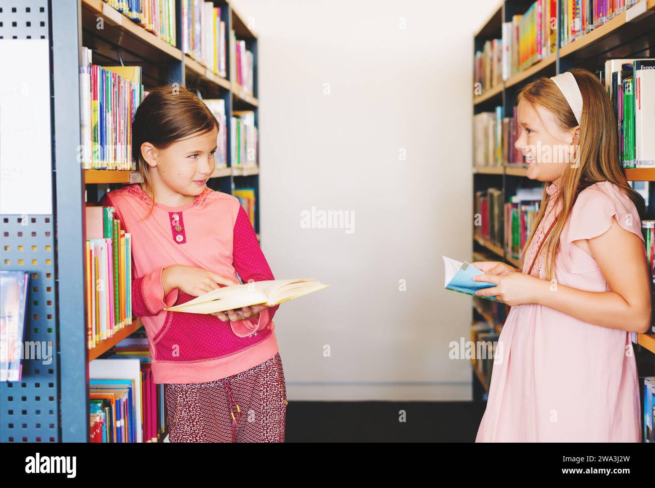 Two little girls reading books in the library Stock Photo - Alamy