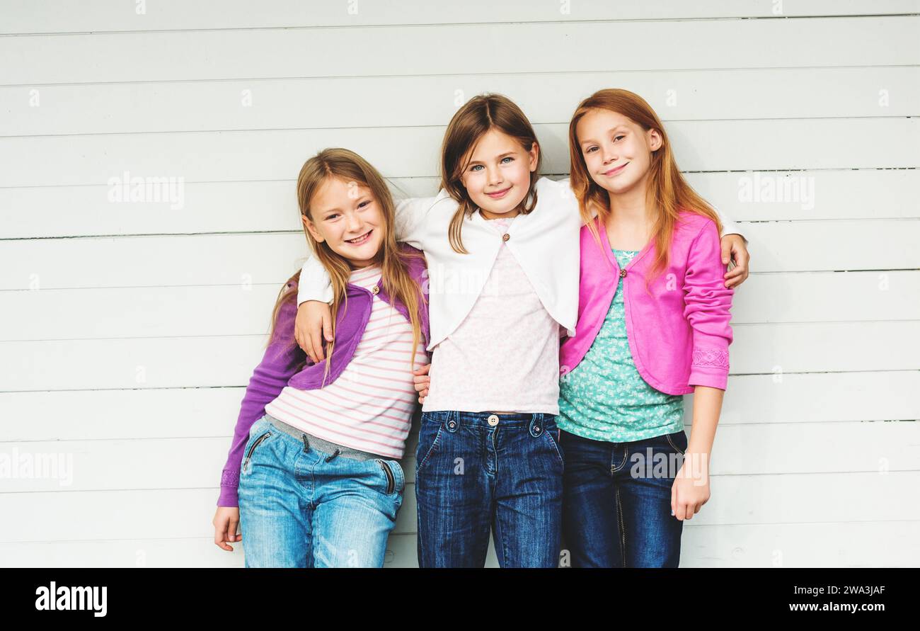 Group of 3 little girls standing outdoors against white wooden ...