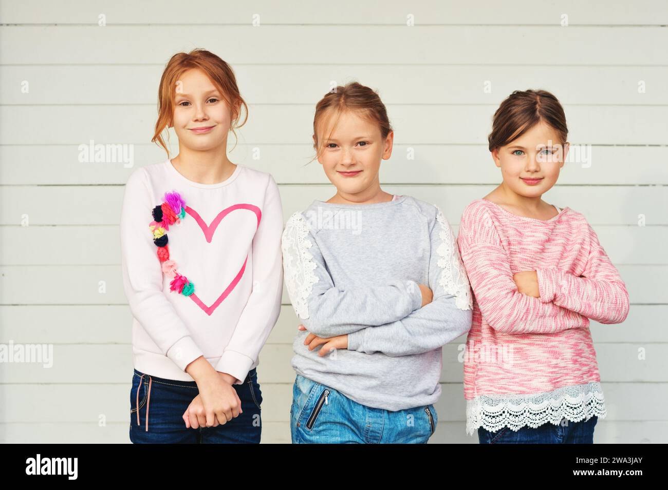 Group of 3 little girls standing outdoors against white wooden ...