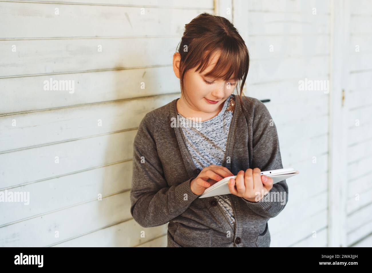 Cute little girl playing with tablet pc, standing against white wooden ...