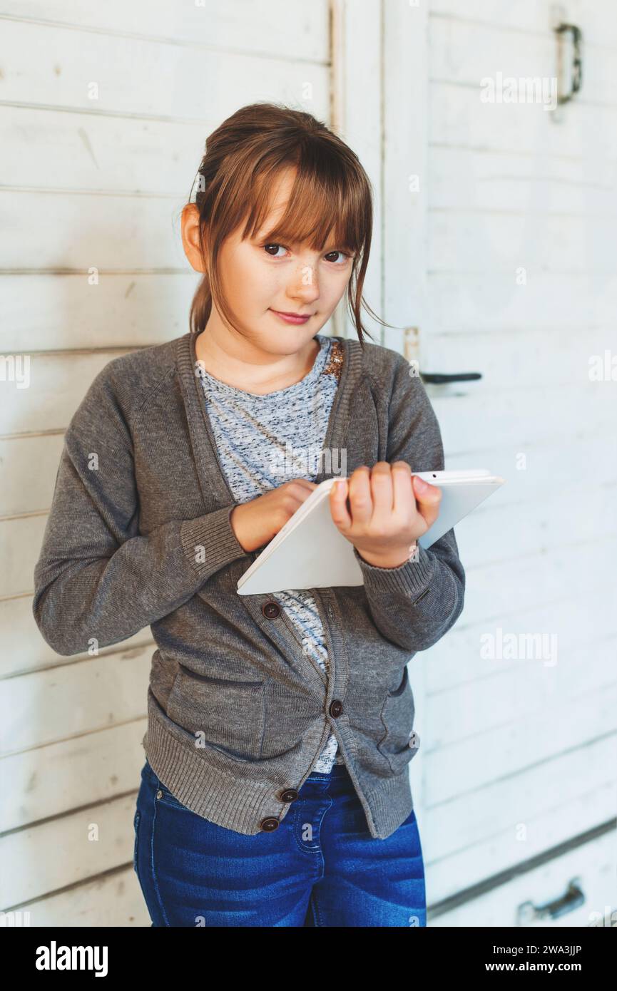 Cute little girl playing with tablet pc, standing against white wooden ...