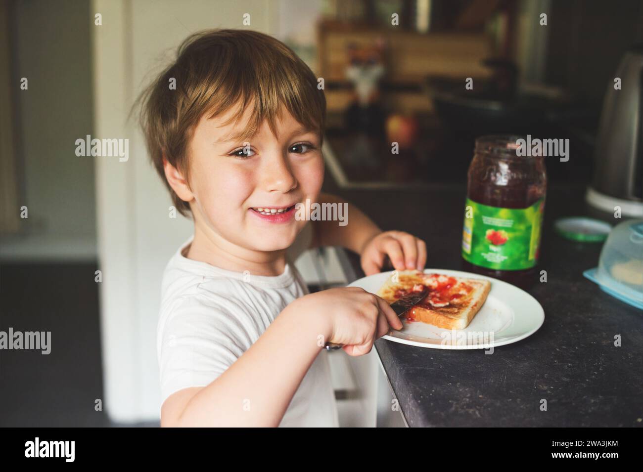 Cute little 6 year old boy preparing alone his toast with butter and ...