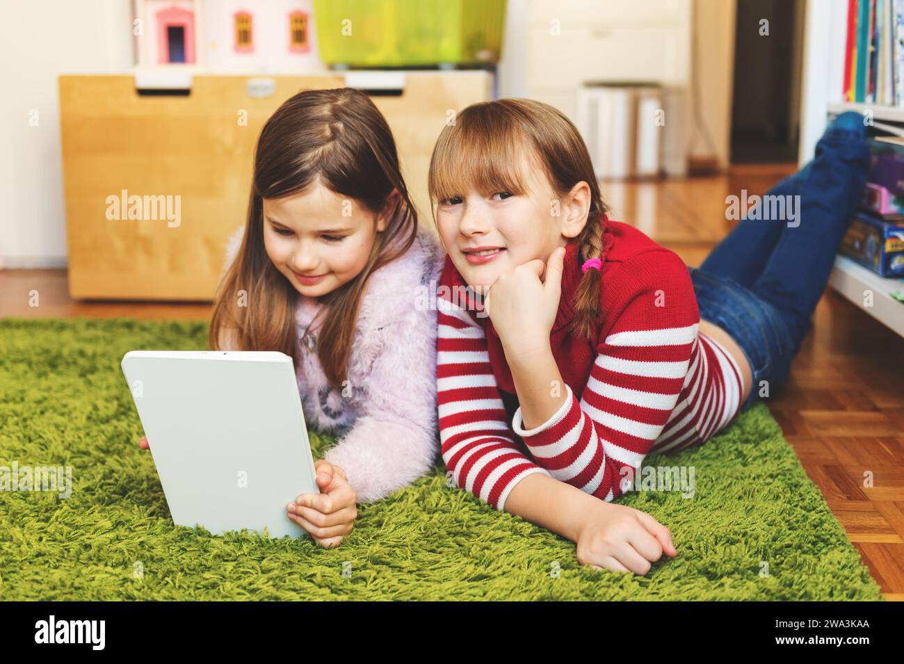 Two cute little girls playing on digital tablet pc, laying on green ...