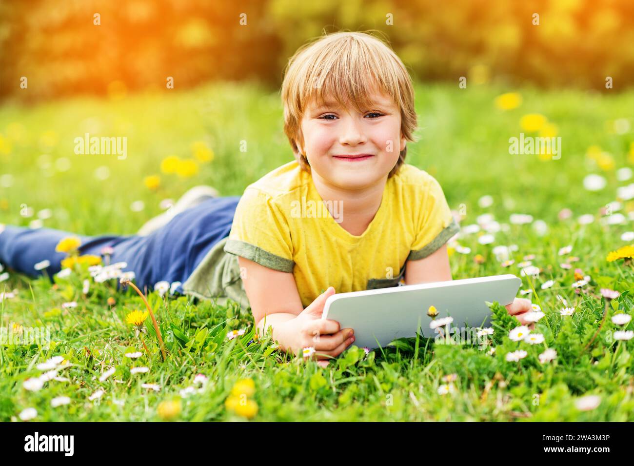Happy little kid boy playing tablet PC outdoors in the park on a very ...