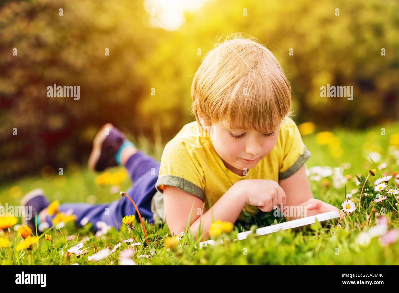 Happy little kid boy playing tablet PC outdoors in the park on a very ...
