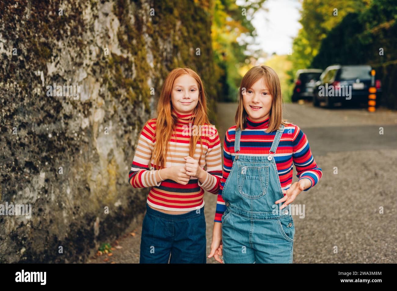 Outdoor portrait of two funny preteen girls wearing denim jeans, stripe ...