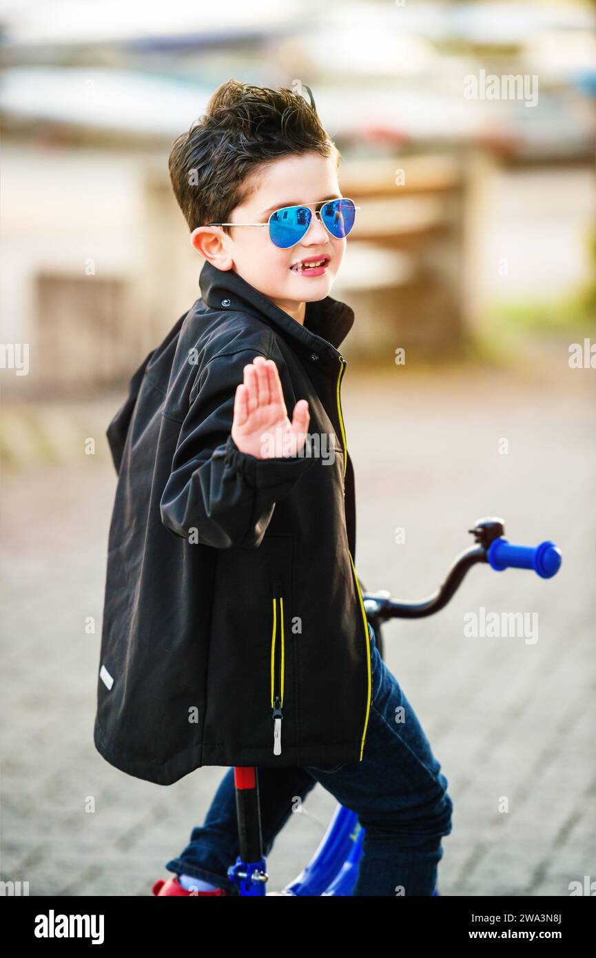 Little kid boy riding a bike, looking back over his shoulder, wearing ...