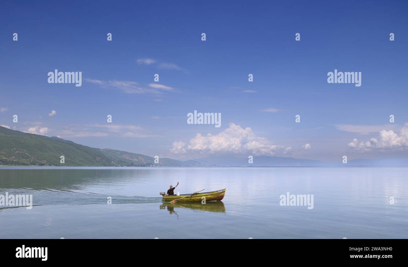 Friendly waving fisherman on a small fishing boat, wide landscape at ...