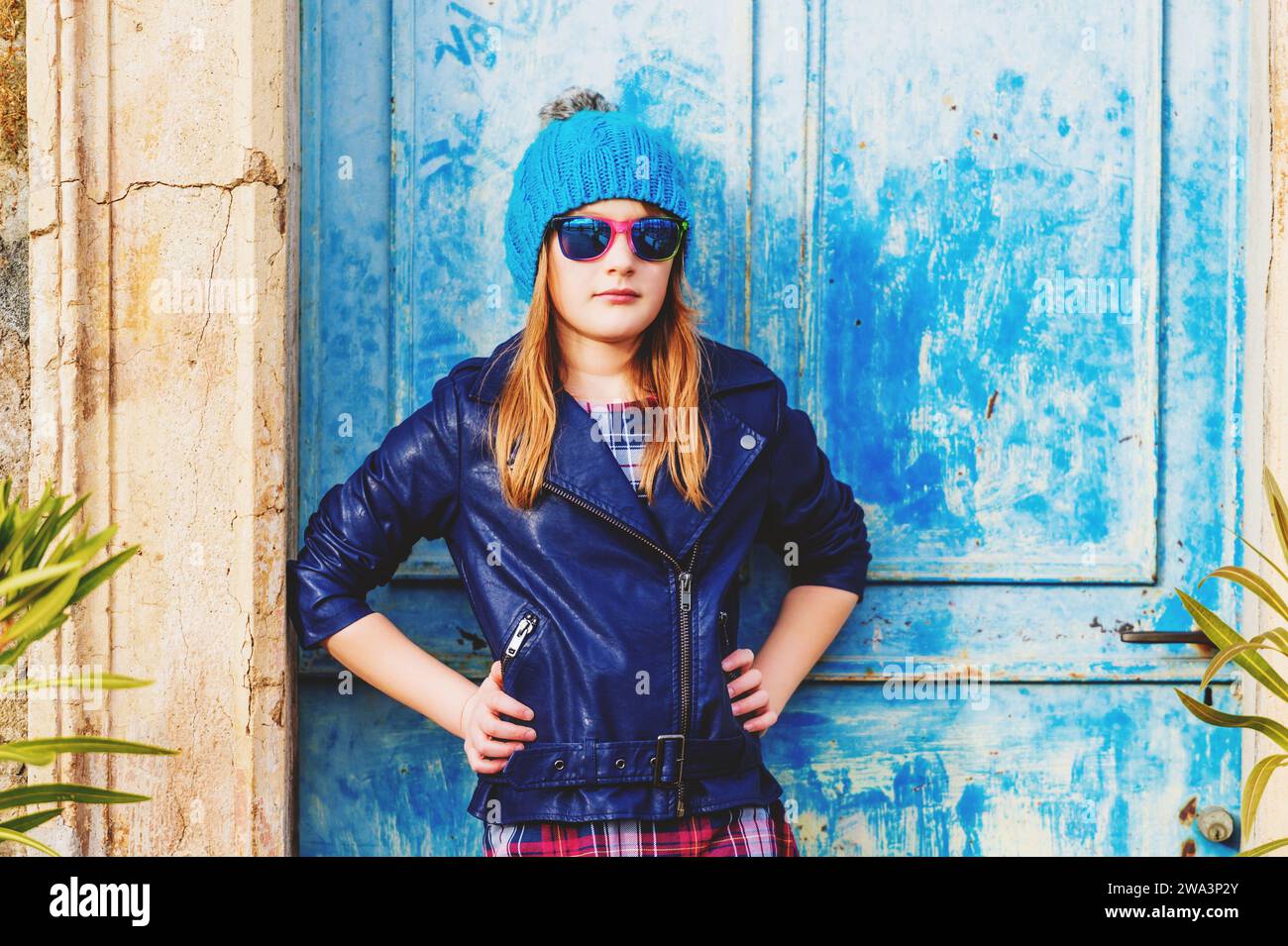 Outdoor fashion portrait of preteen 10-11 years old girl wearing blue leather jacket, hat and ...