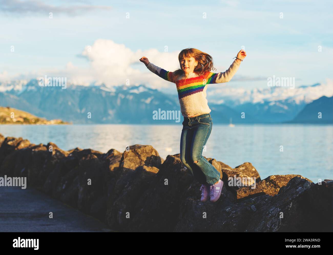 Happy and young kid girl playing next to lake geneva at sunset, arms ...