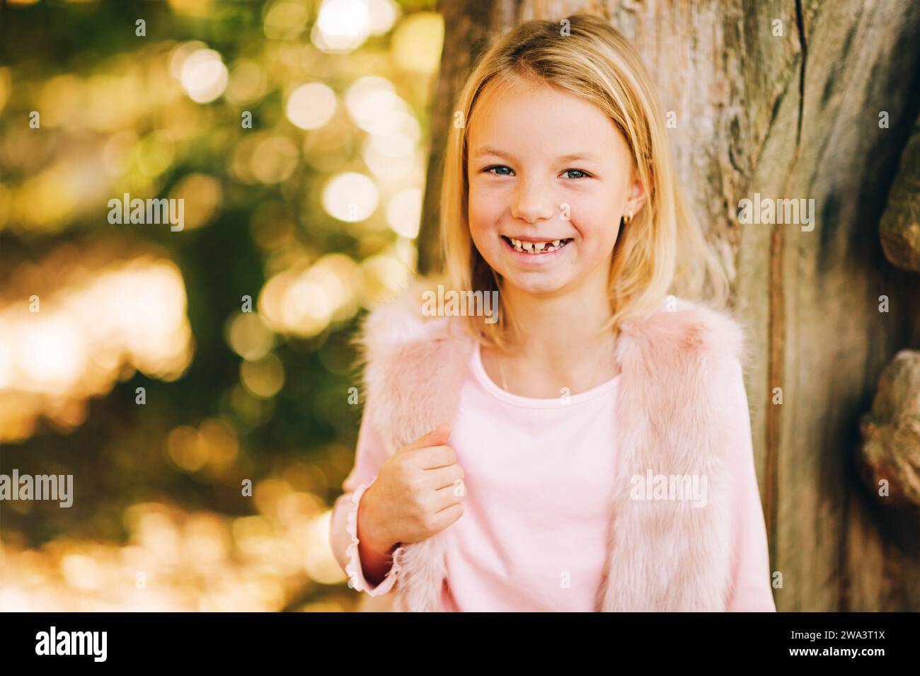 Outdoor portrait of adorable little 7 year old girl, blond hair, blue eyes, wearing pink clothes ...