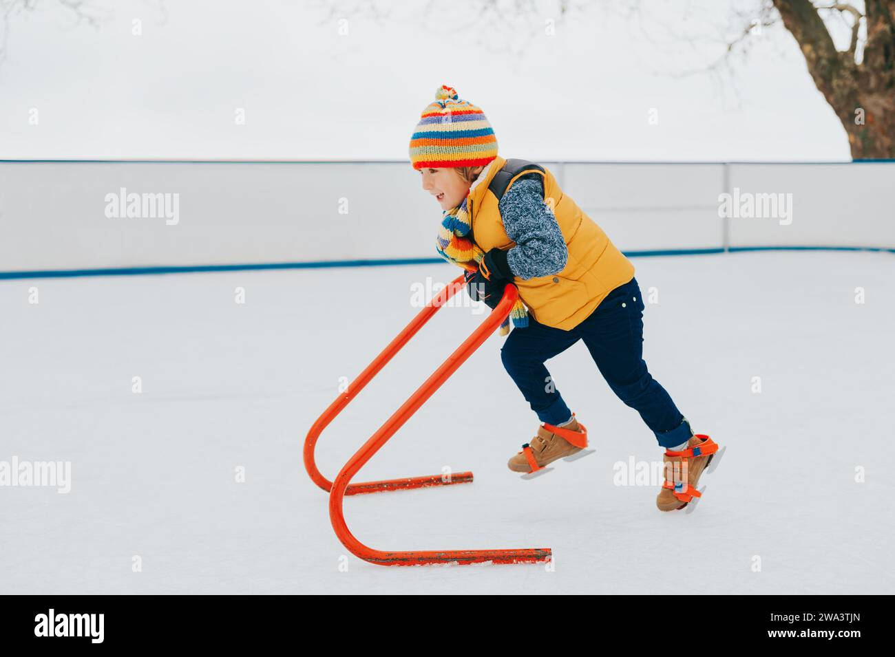 Happy funny little boy practicing with support on skating rink, wearing ...