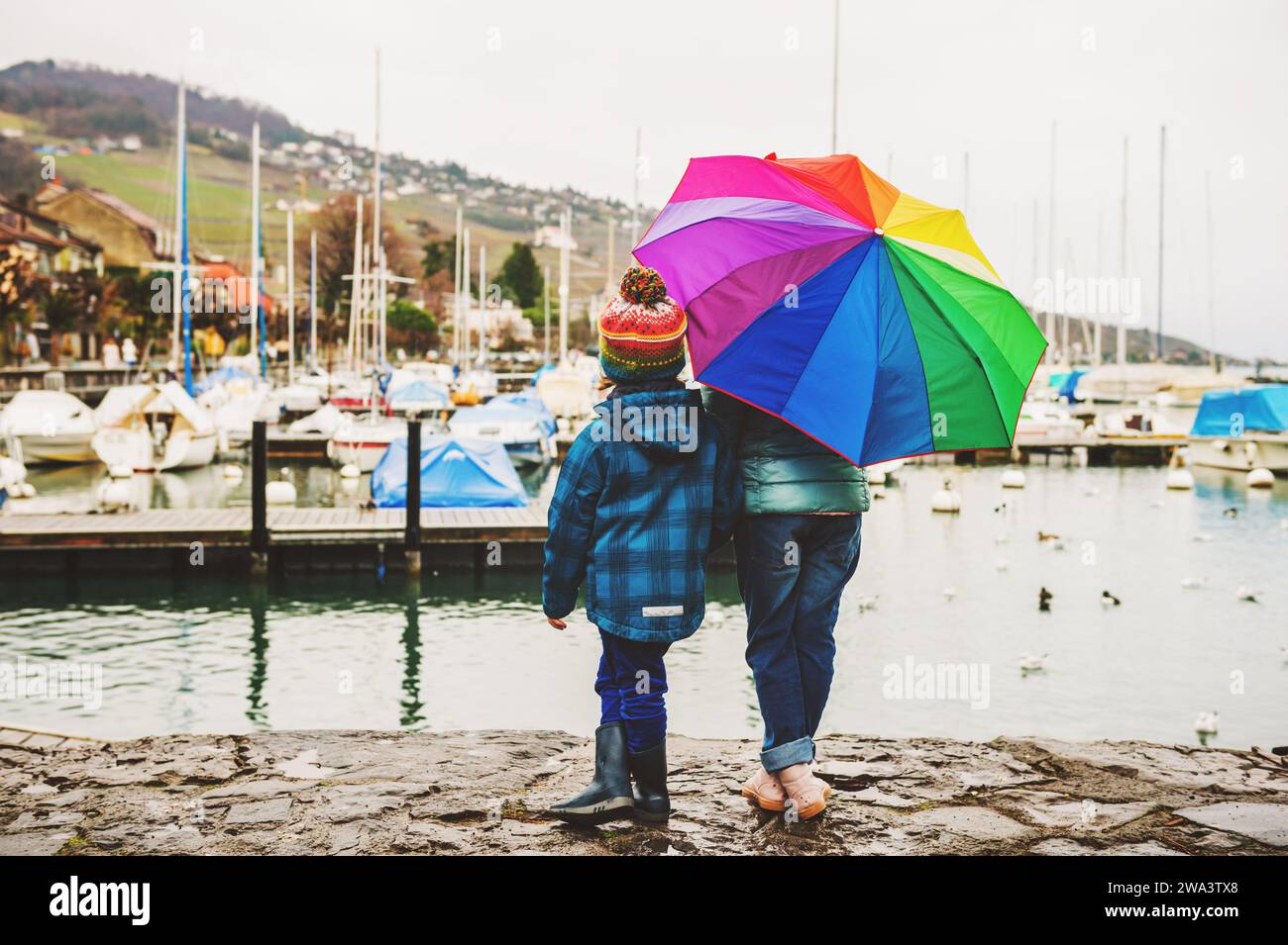 Two cute kids resting by the lake on a rainy day, hiding under big ...