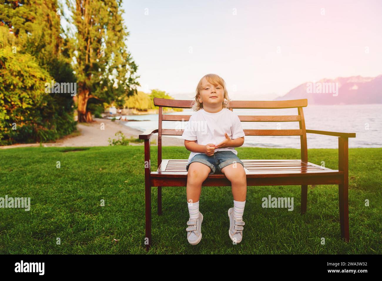 Cute toddler boy playing outdoors, resting on the bench by Lake Geneva ...