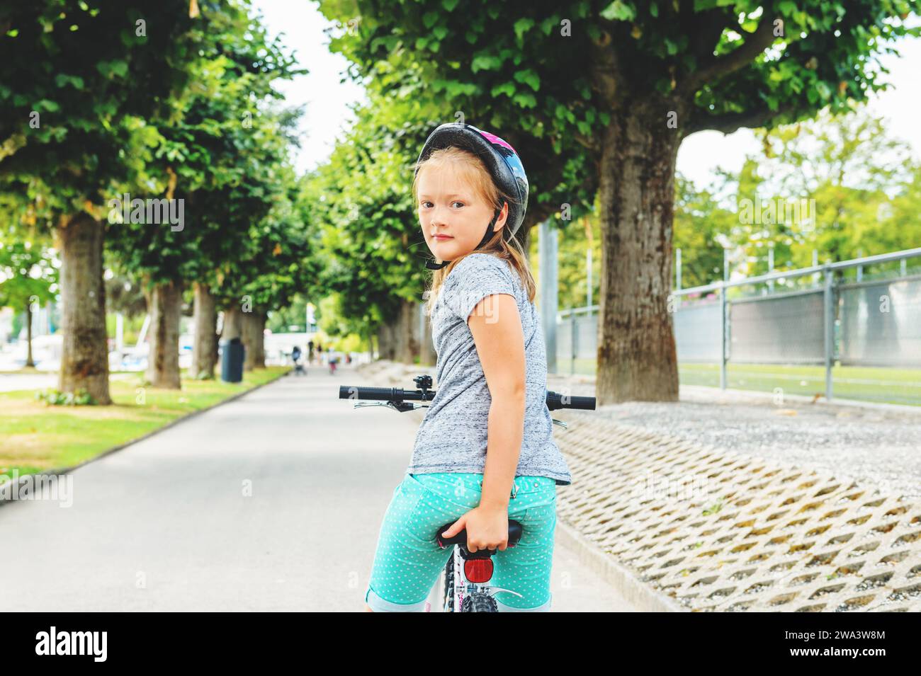 Kid girl sitting on the bicycle in the park, looking back over the ...