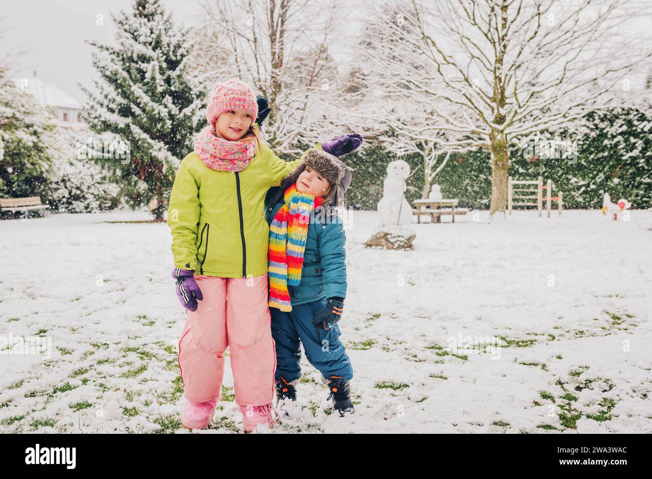 Two adorable kids playing together in snow park, wearing warm winter ...