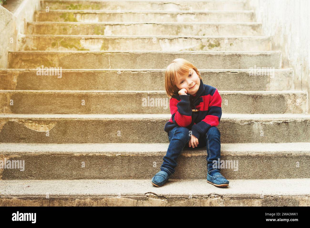 Adorable little boy sitting on stairs in a city, wearing red and blue ...