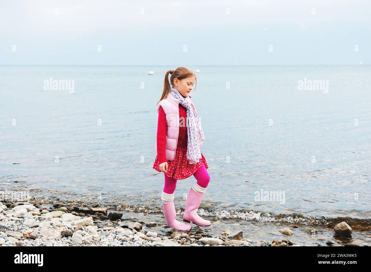 Cute little girl walking by the lake on a cold cloudy day, wearing pink ...