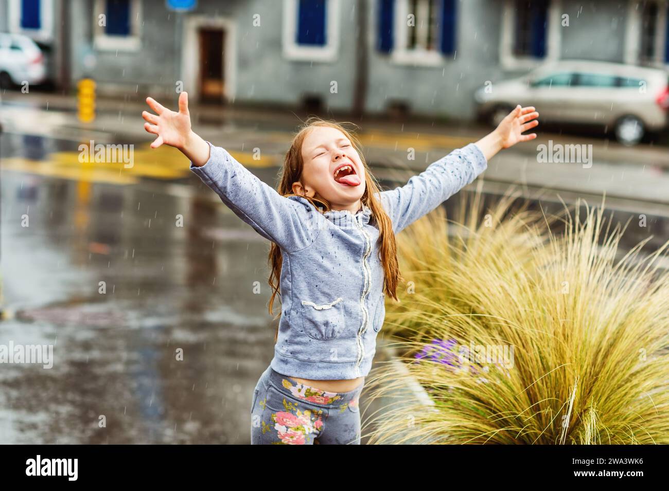 Adorable little girl catching rain drops with her tongue, arms wide ...