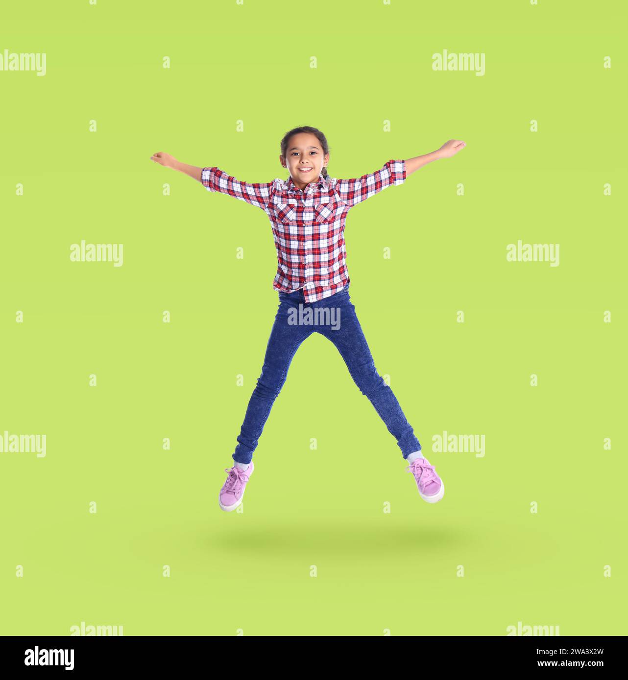 Cute girl jumping on yellowish green background Stock Photo - Alamy