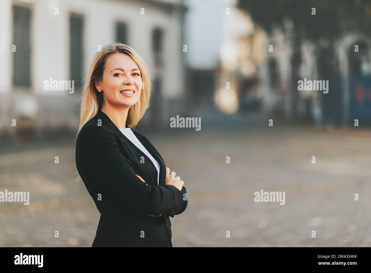 Portrait of beautiful blond woman, wearing black jacket, arms crossed ...