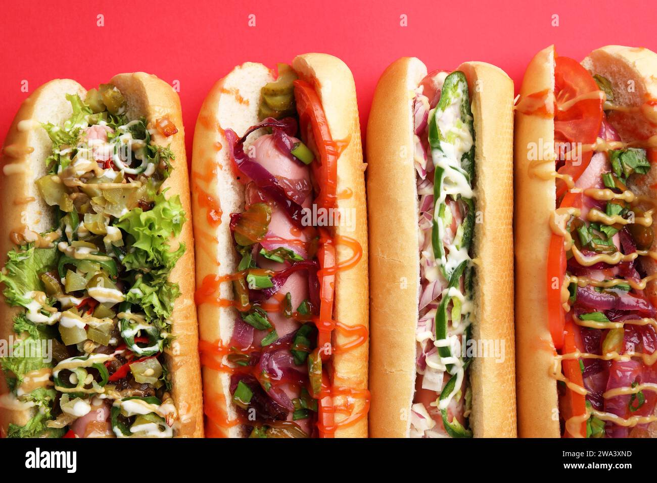 Delicious hot dogs with different toppings on red background, flat lay ...