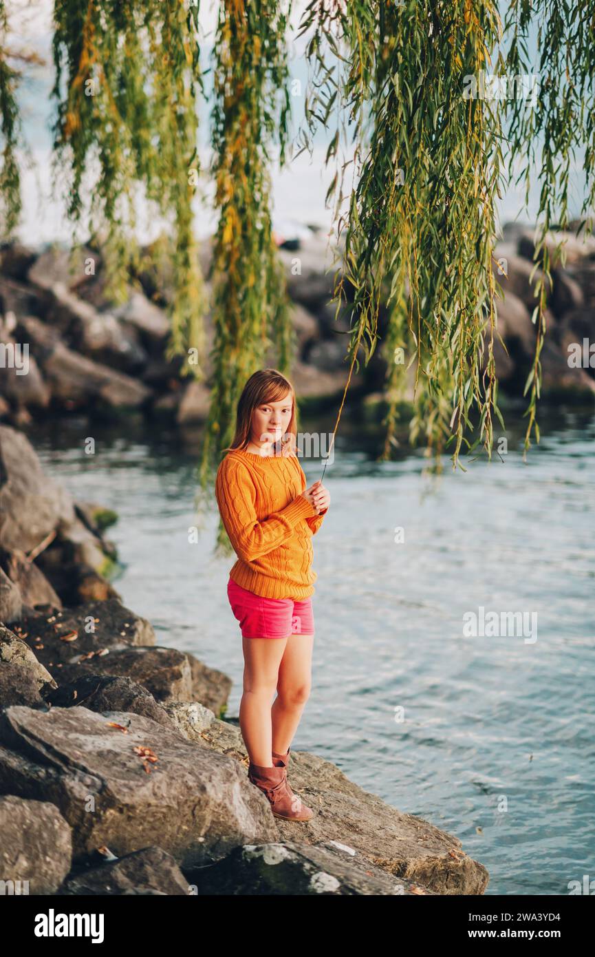 Outdoor portrait of cute preteen kid girl playing by the lake at sunset ...
