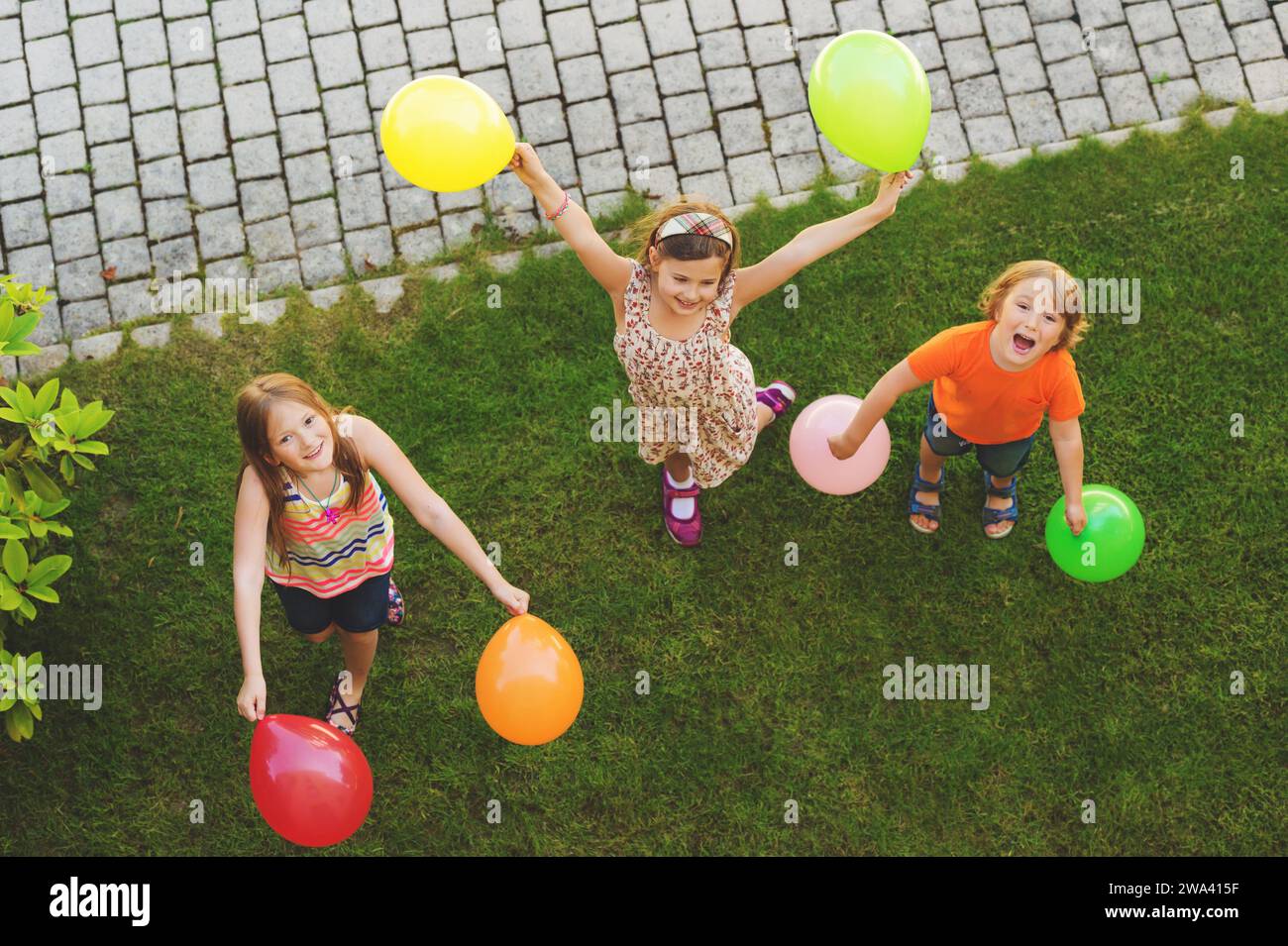 Three happy little kids playing with colorful balloons outdoors, top ...