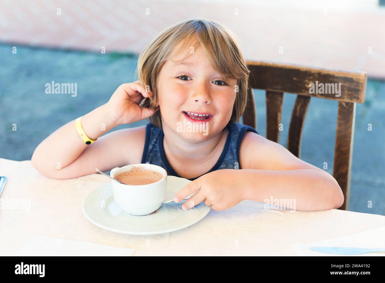 Outdoor portrait of a cute little boy drinking hot chocolate in cafe ...