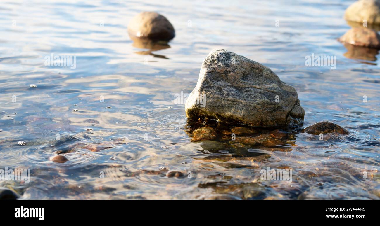 Round stones in the shore water on a calm and clear day in the ...